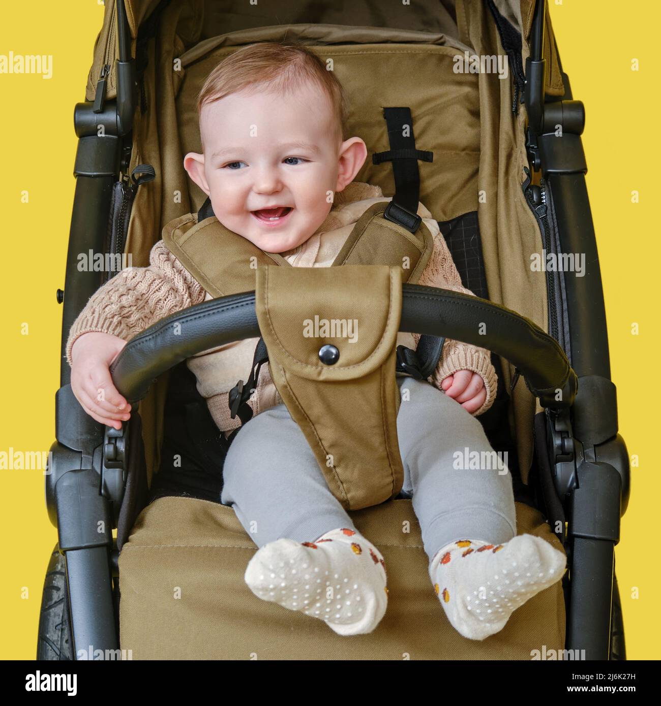 A happy child is sitting in a baby carriage on a studio yellow ...