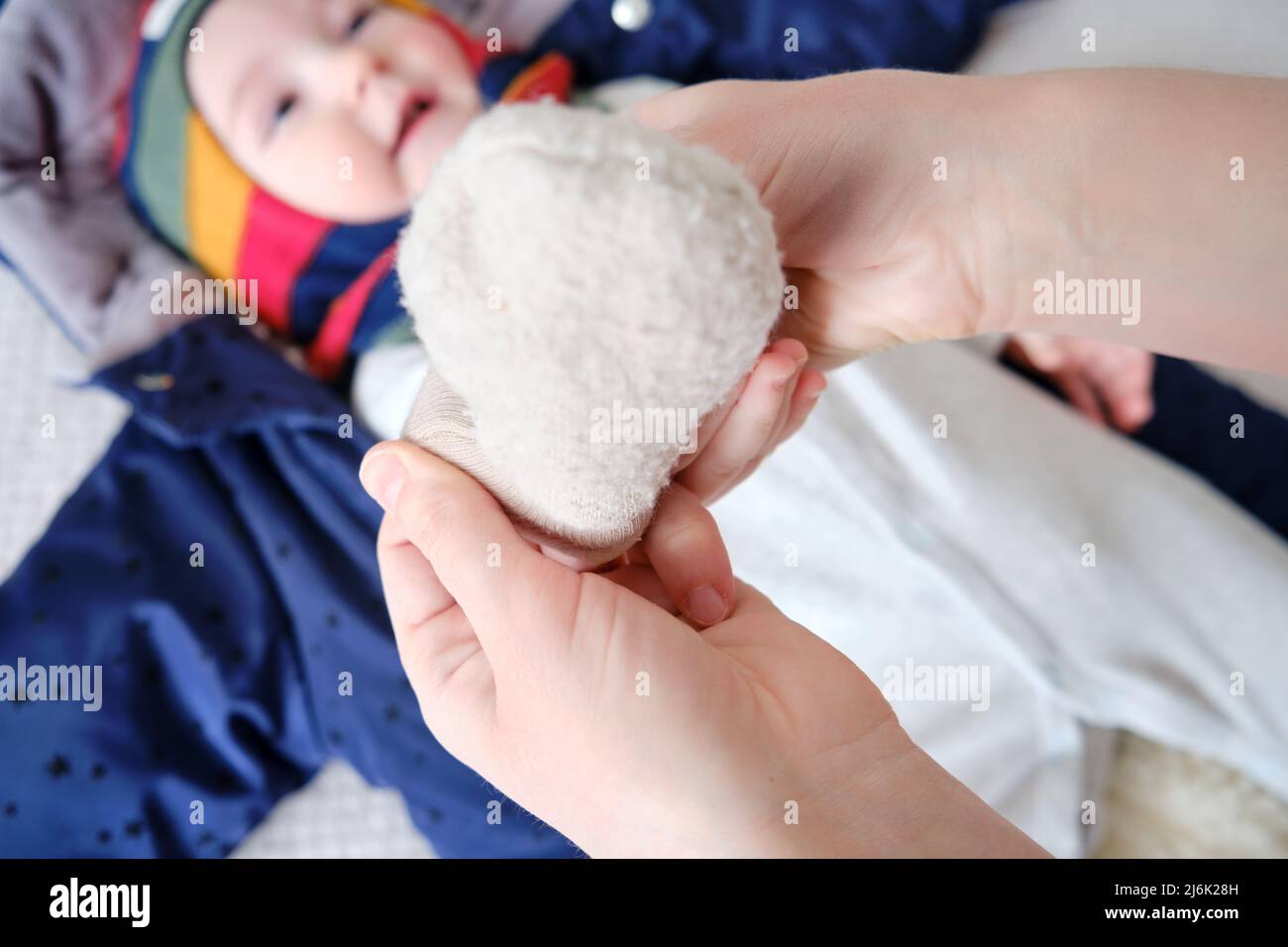 A mother woman puts on warm mittens for a baby boy. Mom dresses a happy ...