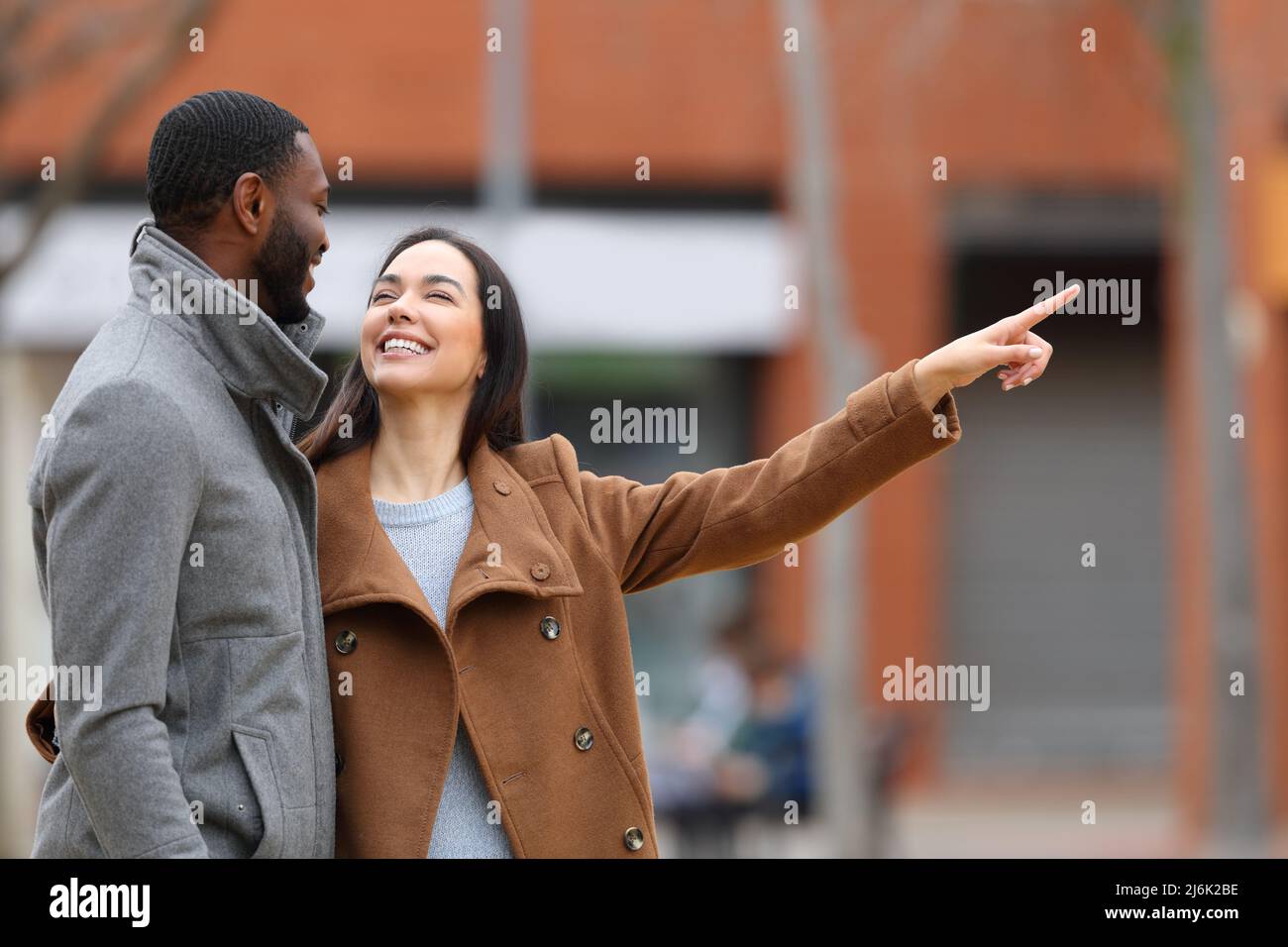 Interracial couple talking and pointing walking in the street in winter ...