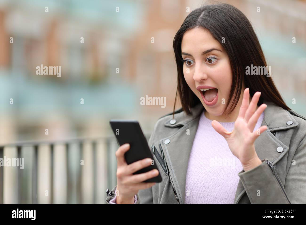 Surprised woman checking cell phone content in the street Stock Photo - Alamy