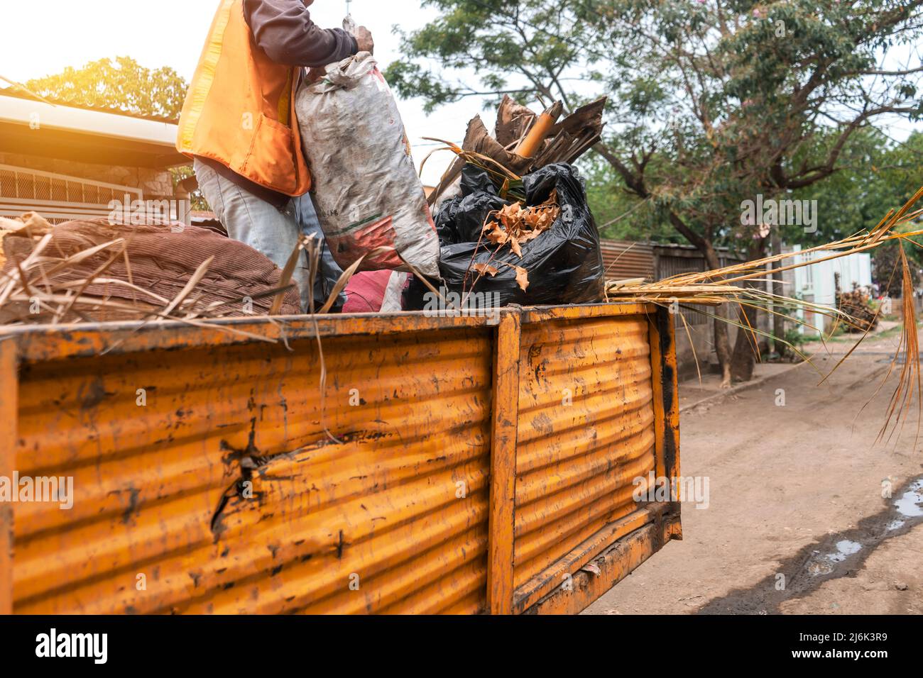 A municipal worker collecting garbage on top of a truck in a poor ...