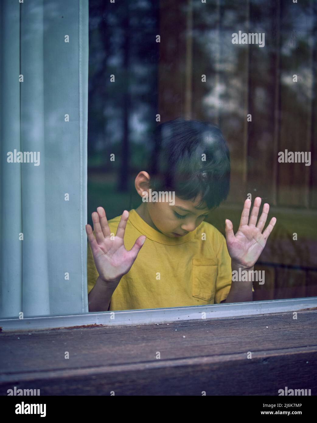 Alone latino child leaning his hands behind the glass of the window ...