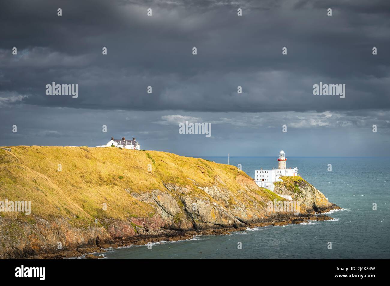 Dark storm clouds and Baily Lighthouse illuminated by fleeting sunlight ...