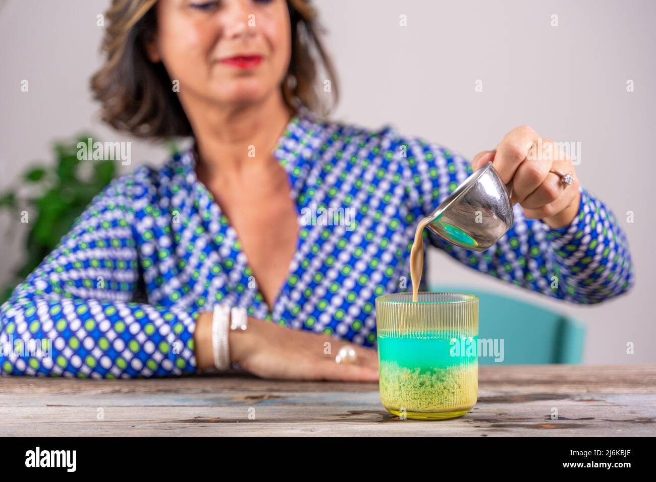 woman dressed in blue shirt sitting pouring liquid into a yellow glass ...