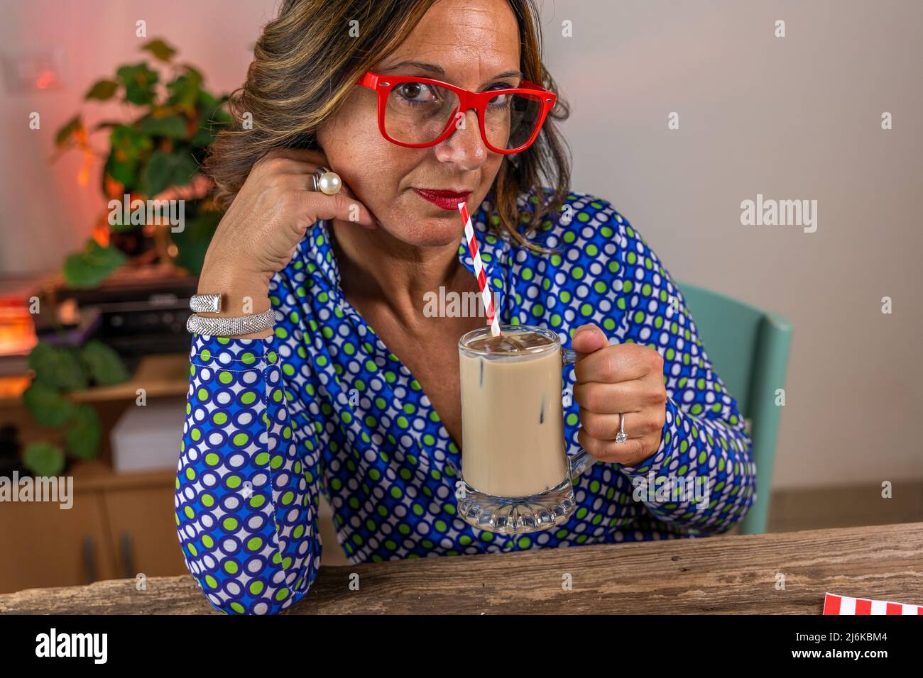 woman dressed in blue shirt and red glasses sitting drinking cold ...