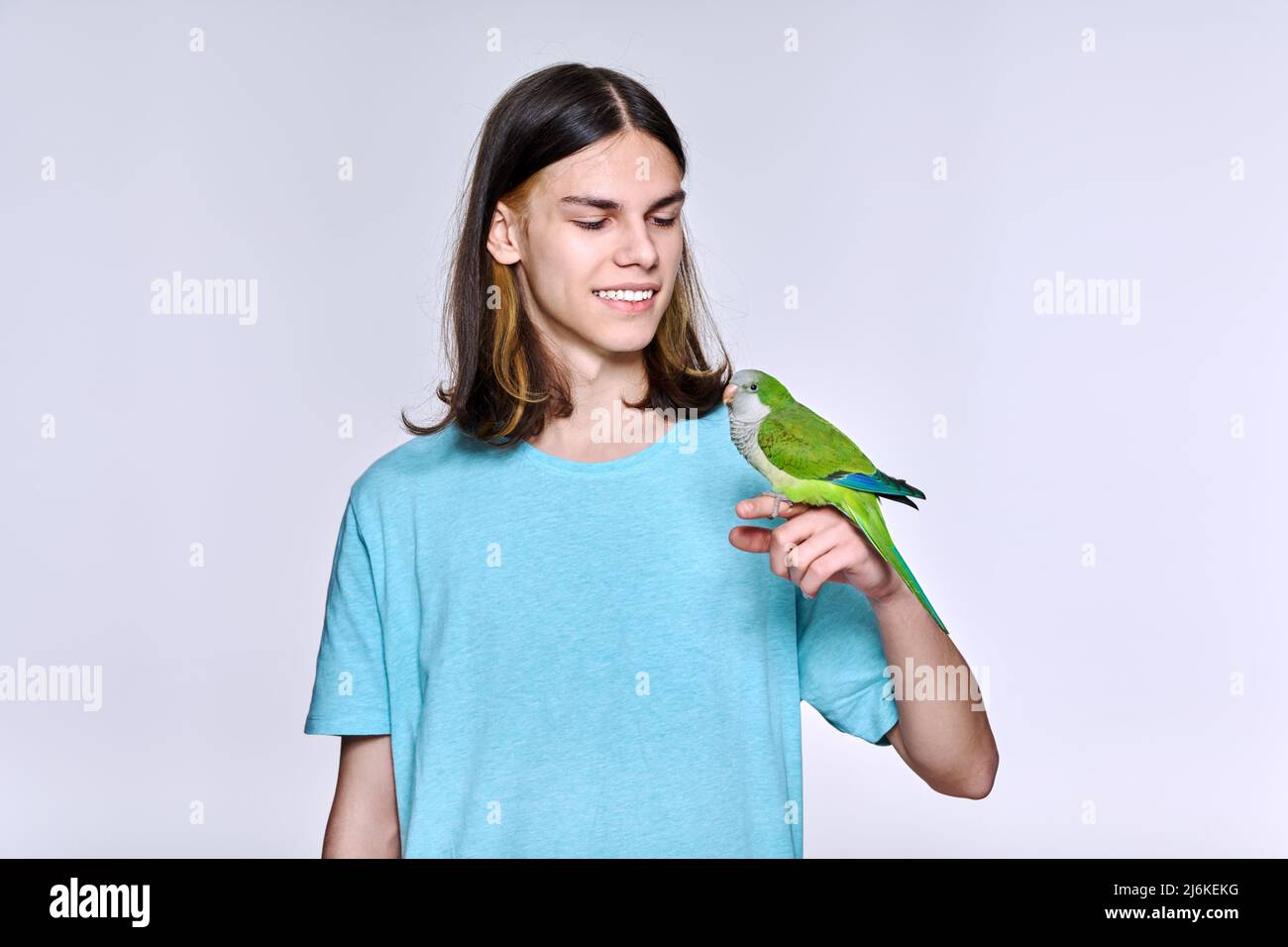 Young male with domestic green Quaker parrot on light studio background ...