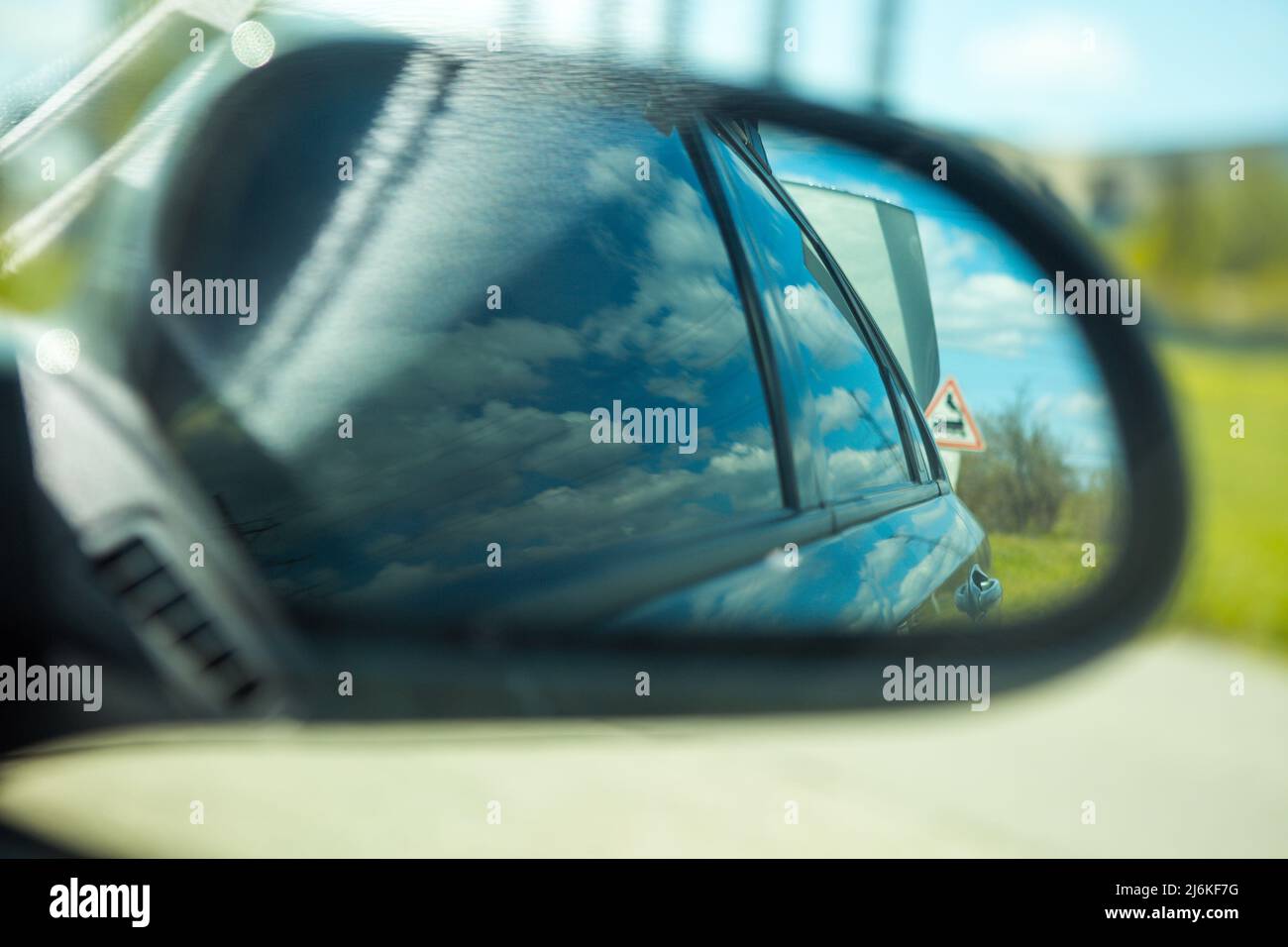 Photo of the side mirror in motion. A road sign beware of the train is ...