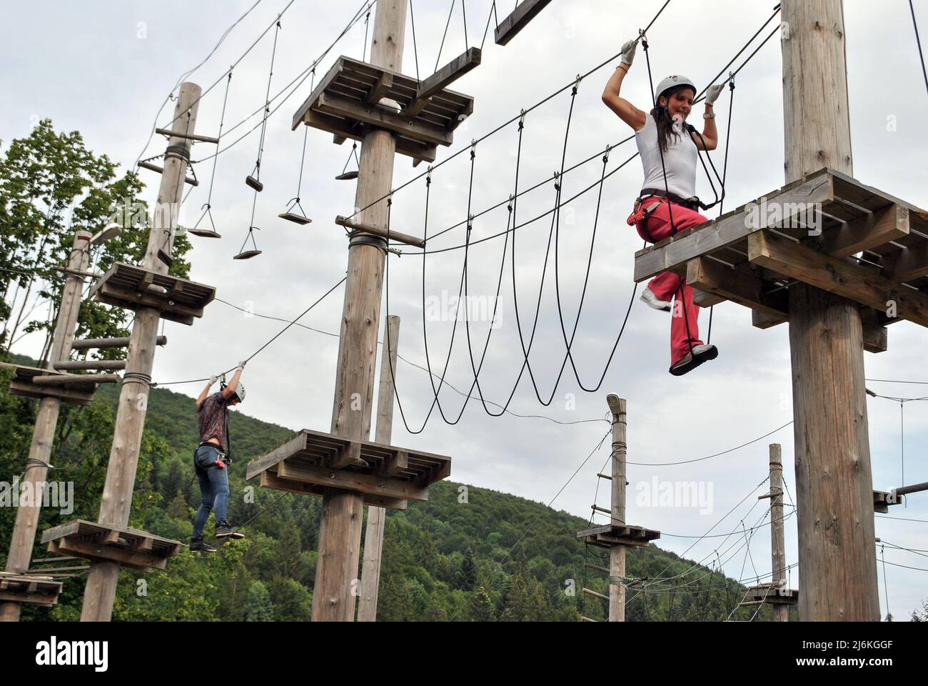 A young woman in a rope amusement park crosses a suspension wooden ...