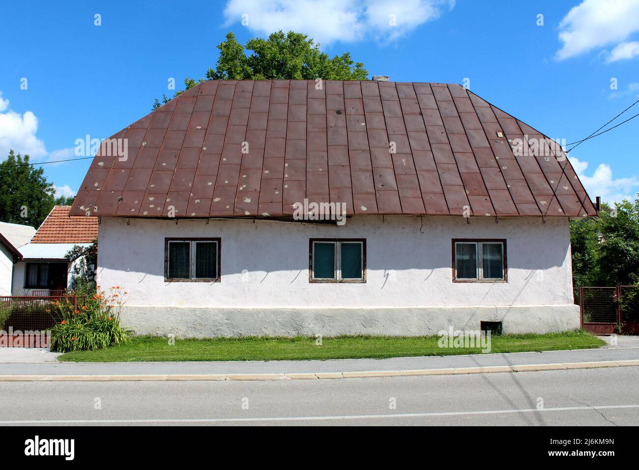 Older small urban family house on concrete foundation with dilapidated white facade around old ...