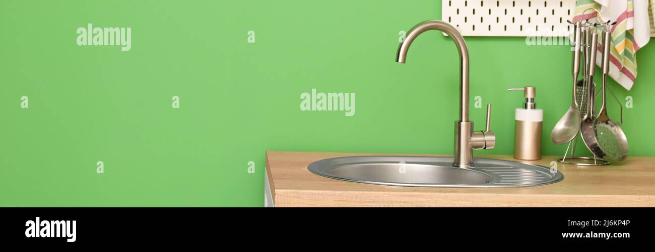 Wooden counter with silver sink and kitchen utensils near green wall ...