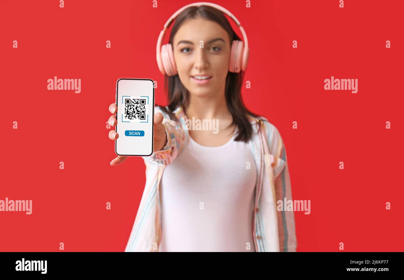 Beautiful young woman in headphones holding smartphone with QR code on ...
