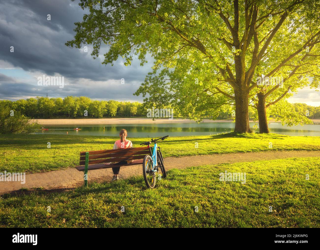 Woman sitting on bench and mountain bike, green trees Stock Photo - Alamy
