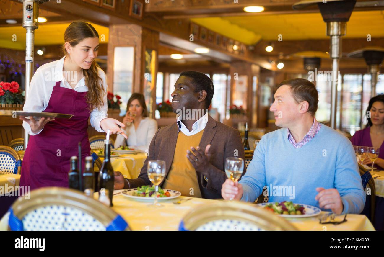 Young waitress politely talking to two men in restaurant Stock Photo ...