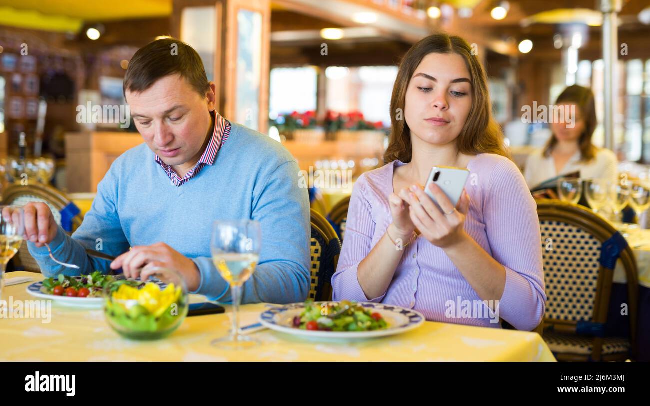 Man and woman look at the screen of his smartphones during lunch in ...