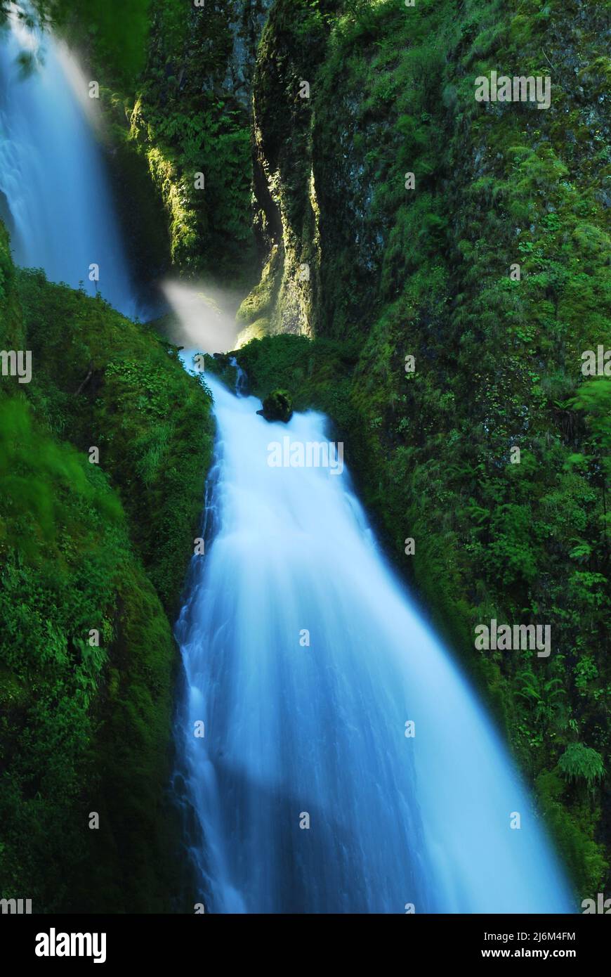 Blue two stage waterfall flowing down a green mountain Stock Photo - Alamy