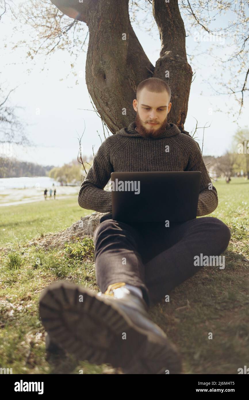 Young man using and typing laptop computer in summer grass Stock Photo ...