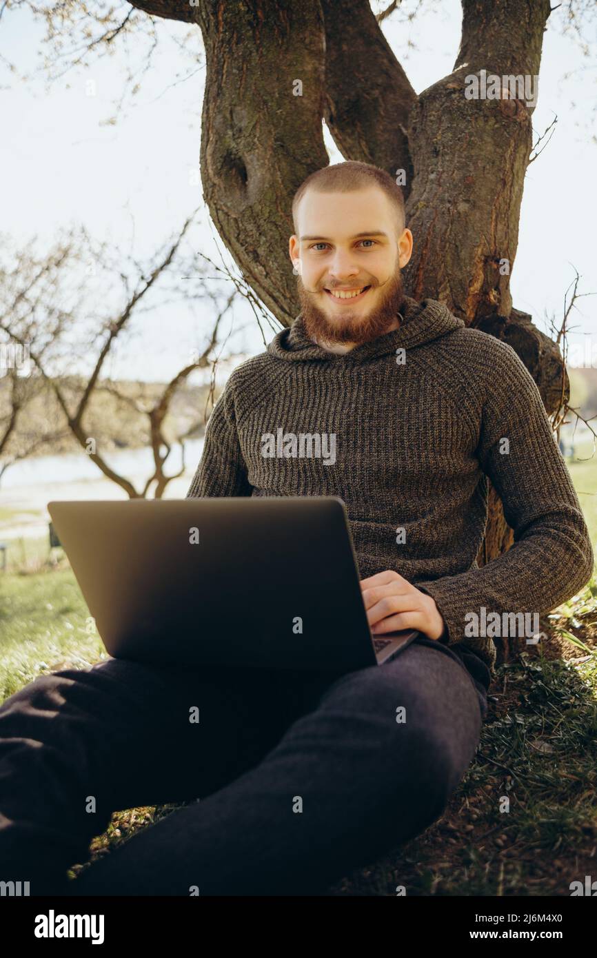 Young man using and typing laptop computer in summer grass Stock Photo ...