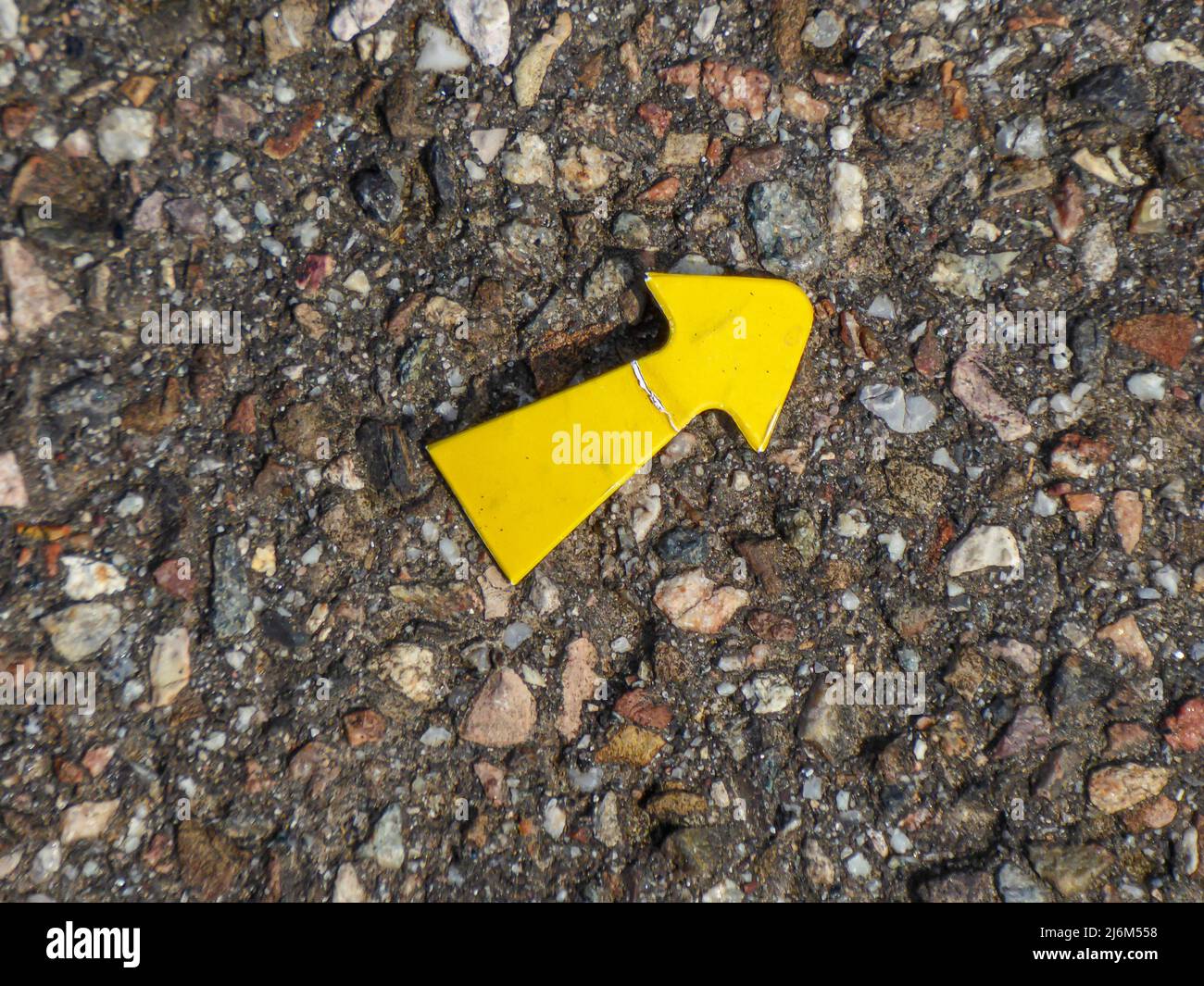 a small, yellow metal arrow with traces of use lies on a rough road ...