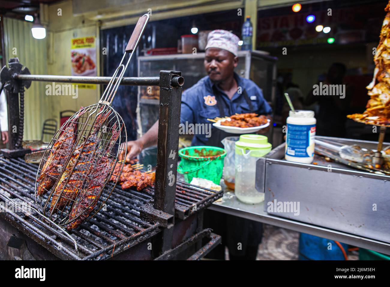 Kenyan chef picks meat skewers from the grill to serve customers during ...
