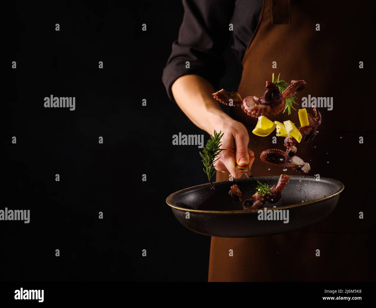 A professional chef cooks octopus with lemon slices in a frying pan on ...