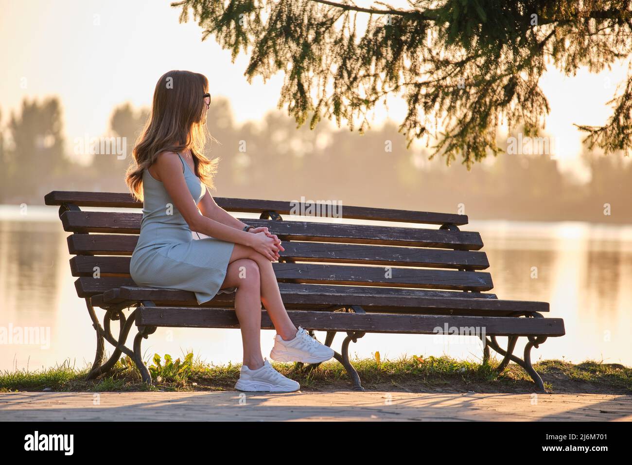 Lonely woman sitting alone on lake shore bench on warm summer evening ...