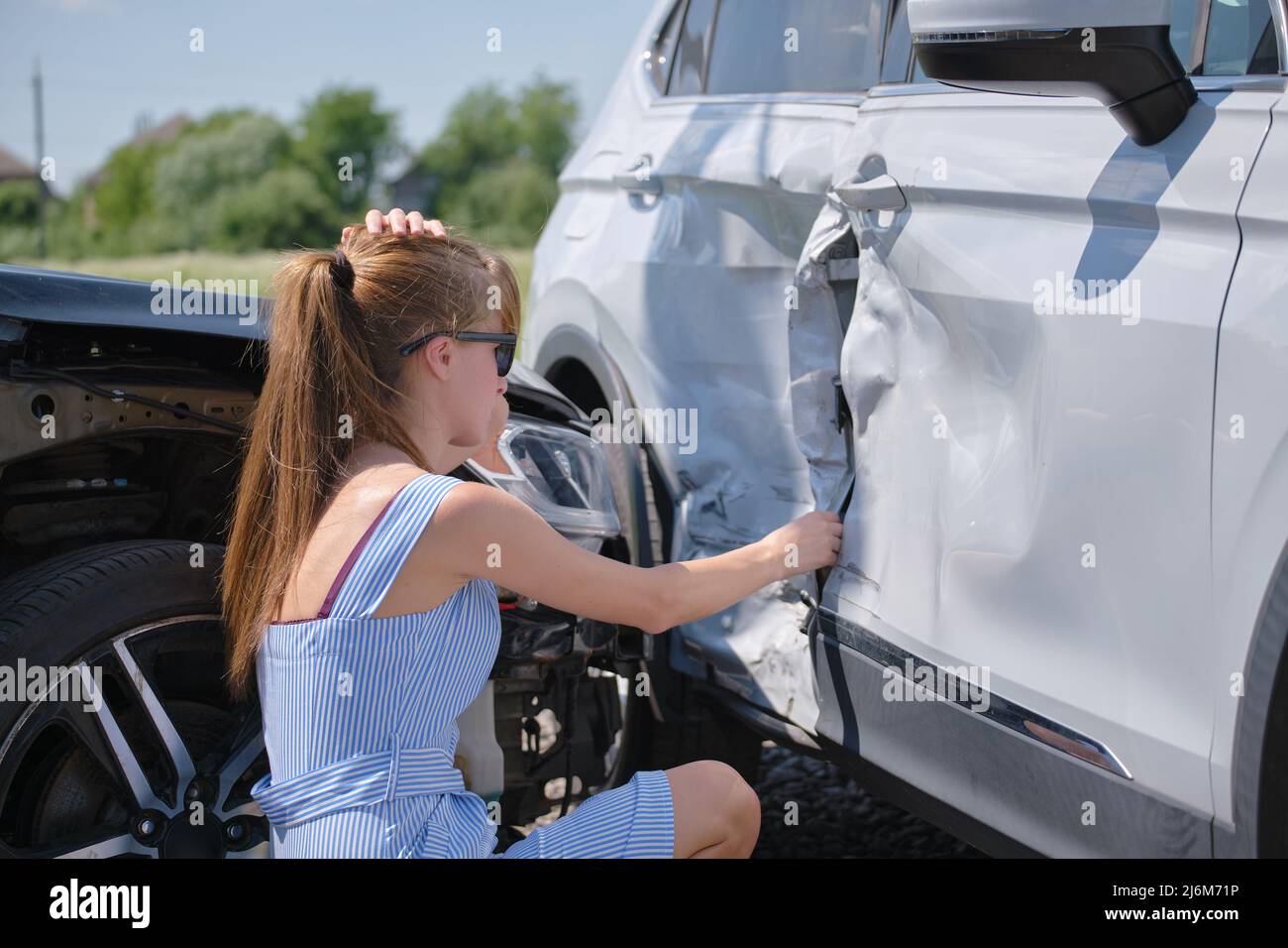 Sad young woman driver sitting near her smashed car looking shocked on ...