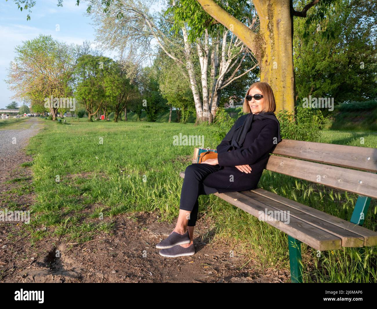 adult mature elegant caucasian woman sitting on a park bench with legs ...
