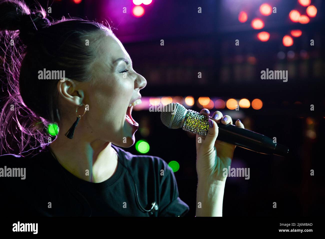 Young singing woman with microphone having fun on open stage in karaoke ...