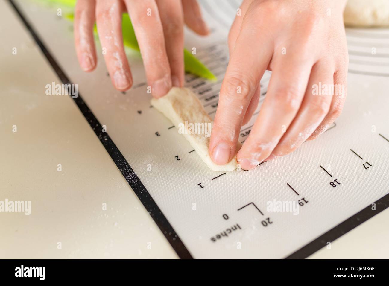 Close-up of hands measuring the length of a piece of dough on a kitchen ...