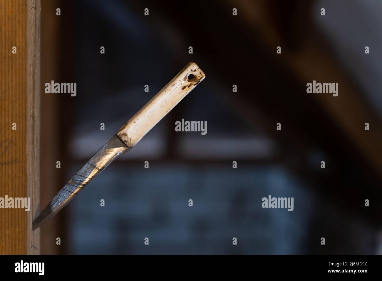 An old sharp knife with a plastic handle stuck into a wooden beam close ...