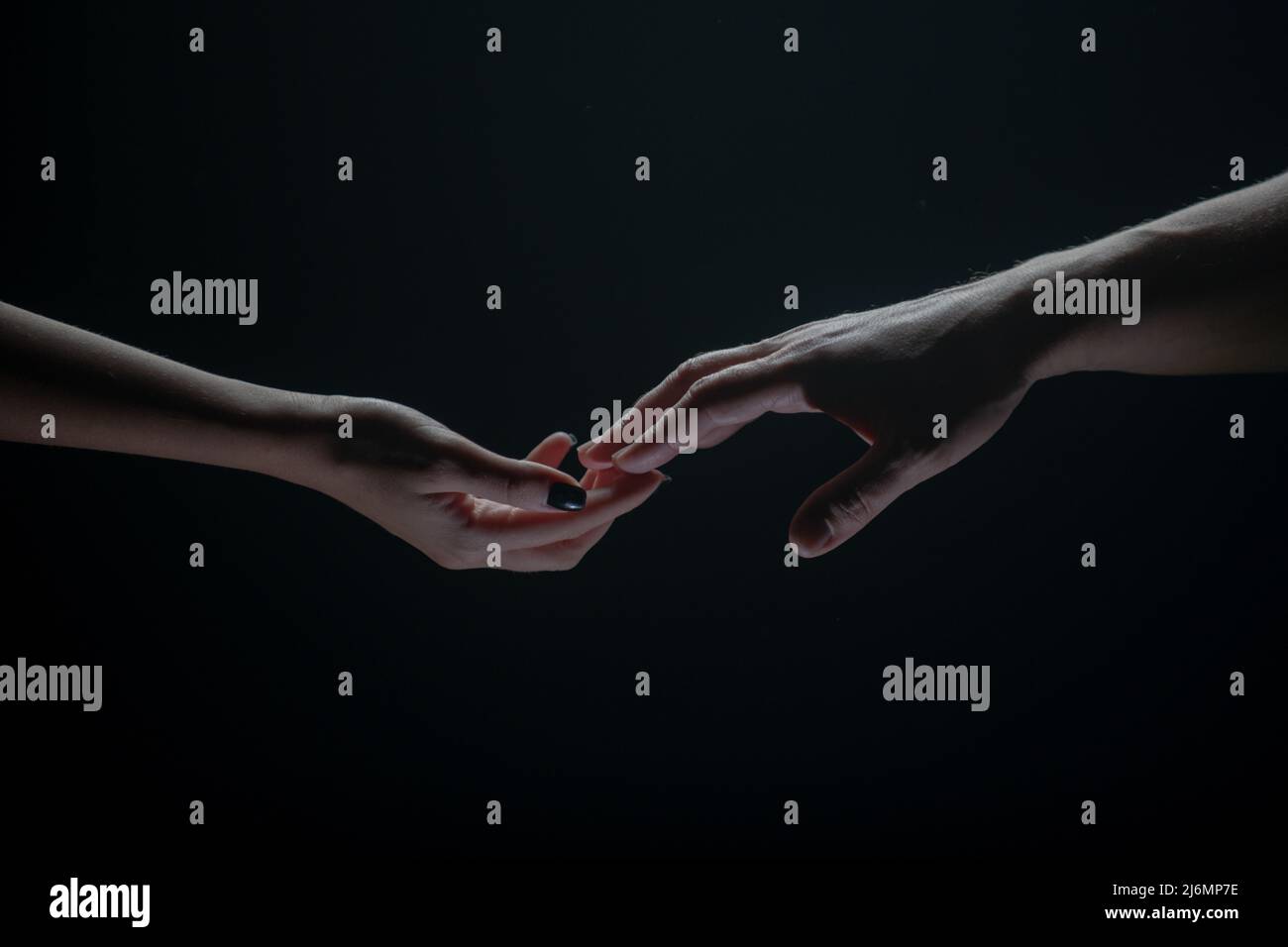 Two hands stretch each other, black background. Couple in love holding ...