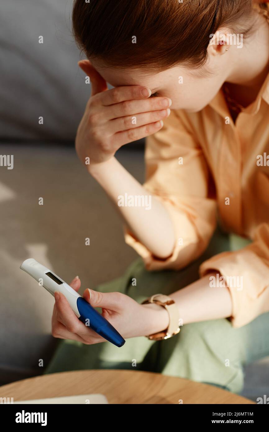 Vertical closeup of crying young woman holding pregnancy test at home ...