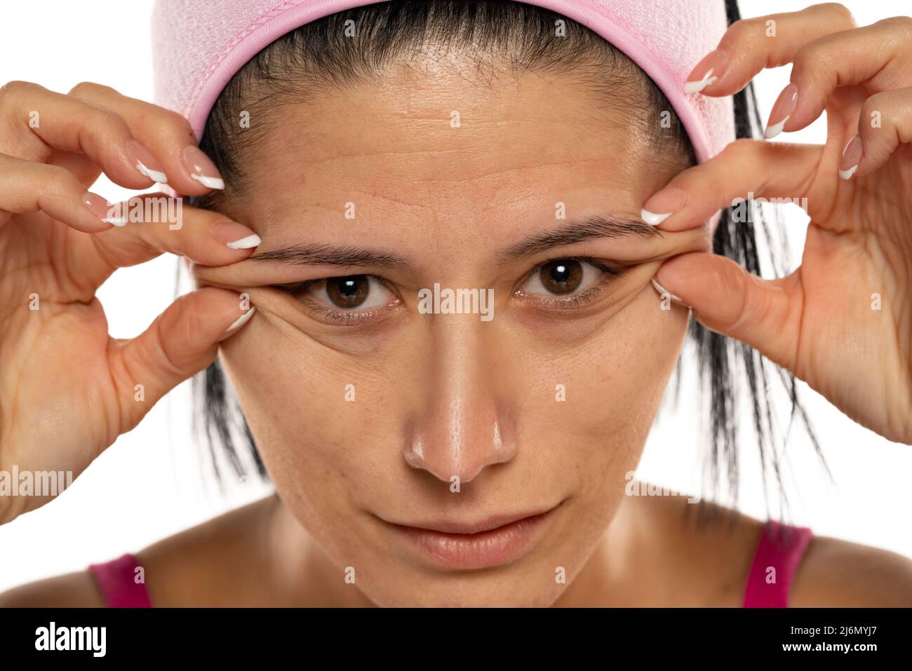 middle-aged woman showing her eye wrinkles with her fingers on a white ...