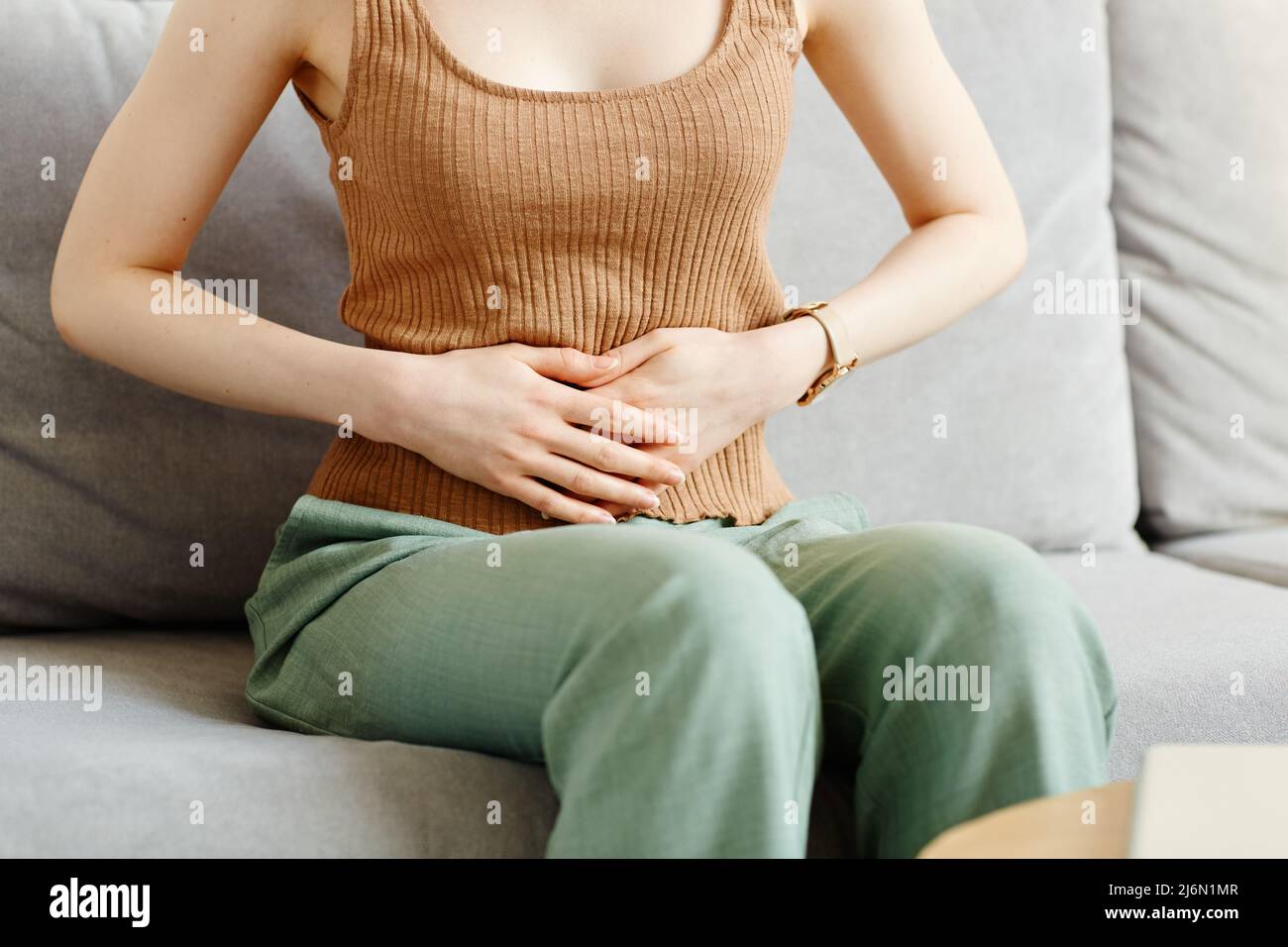 Minimal cropped shot of young woman suffering from cramps holding hands ...