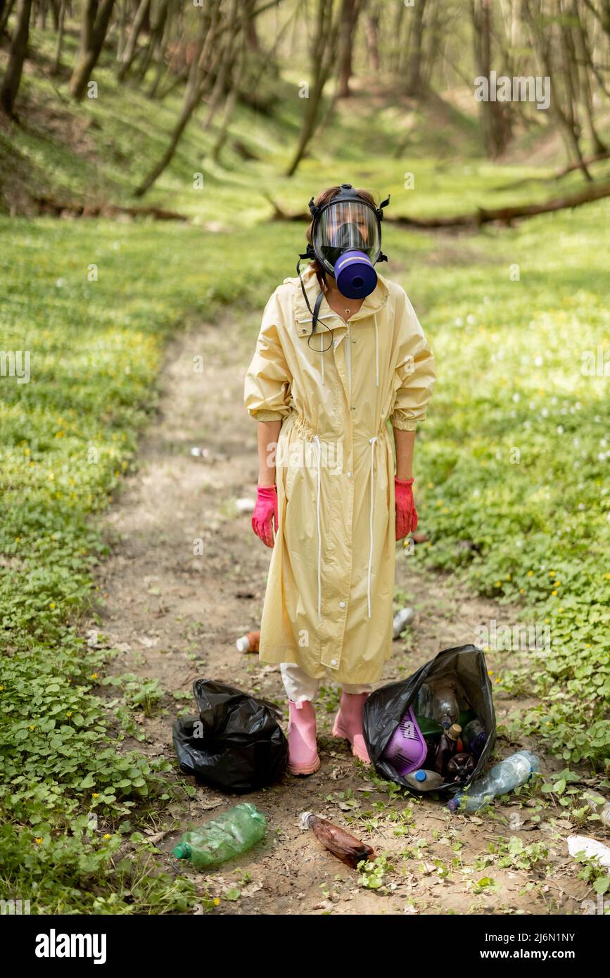 Woman in gas mask and protective clothes collecting scattered plastic ...