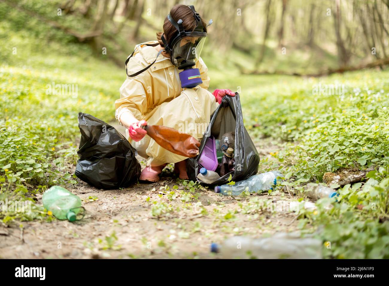 Woman in gas mask and protective clothes collecting scattered plastic ...