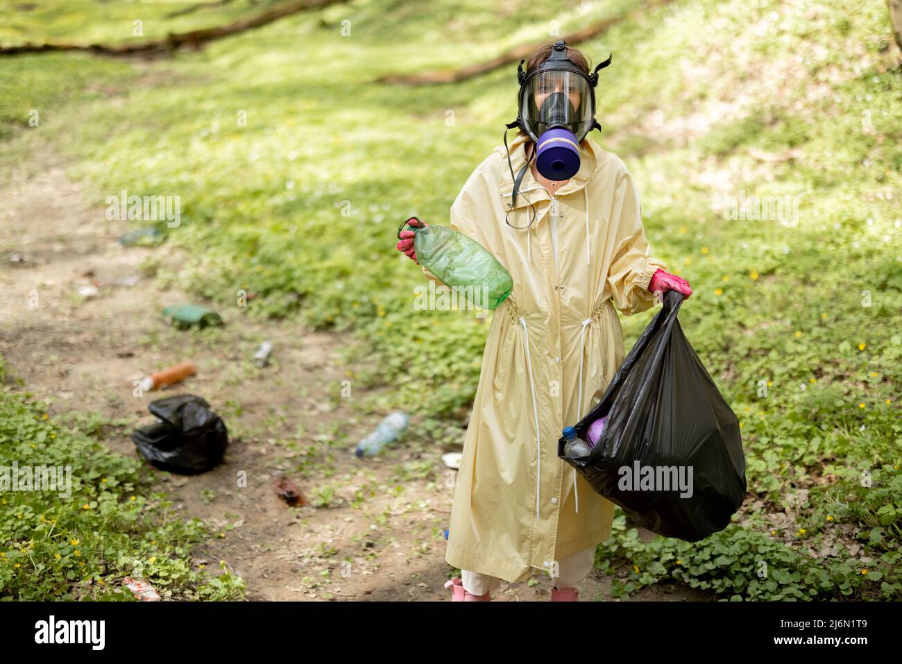 Woman in gas mask and protective clothes collecting scattered plastic ...