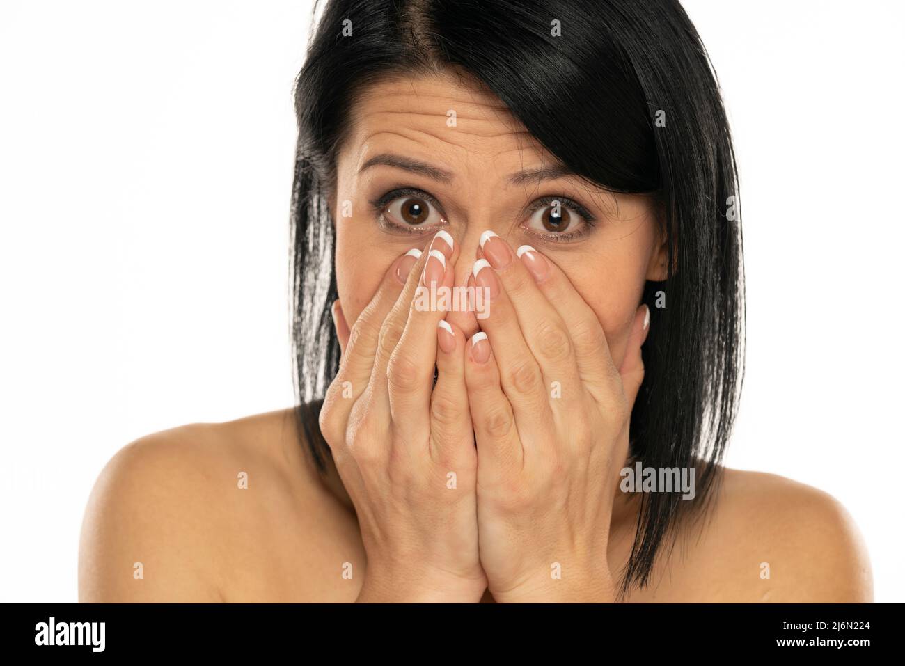 Shocked Young Woman Covers Her Mouth With Her Hands On A White