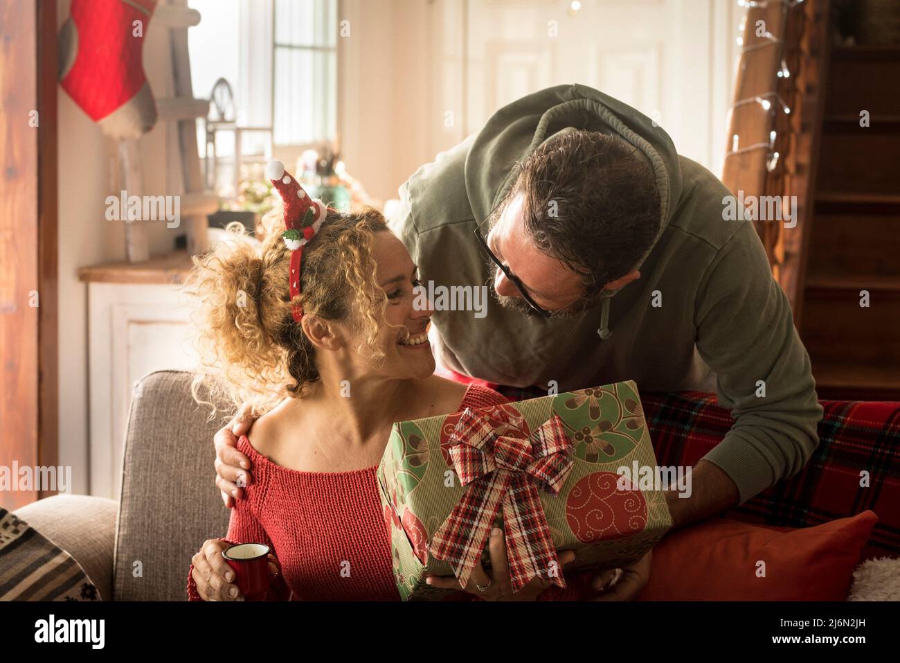 Romantic husband giving gift box to wife sitting on sofa in living room ...