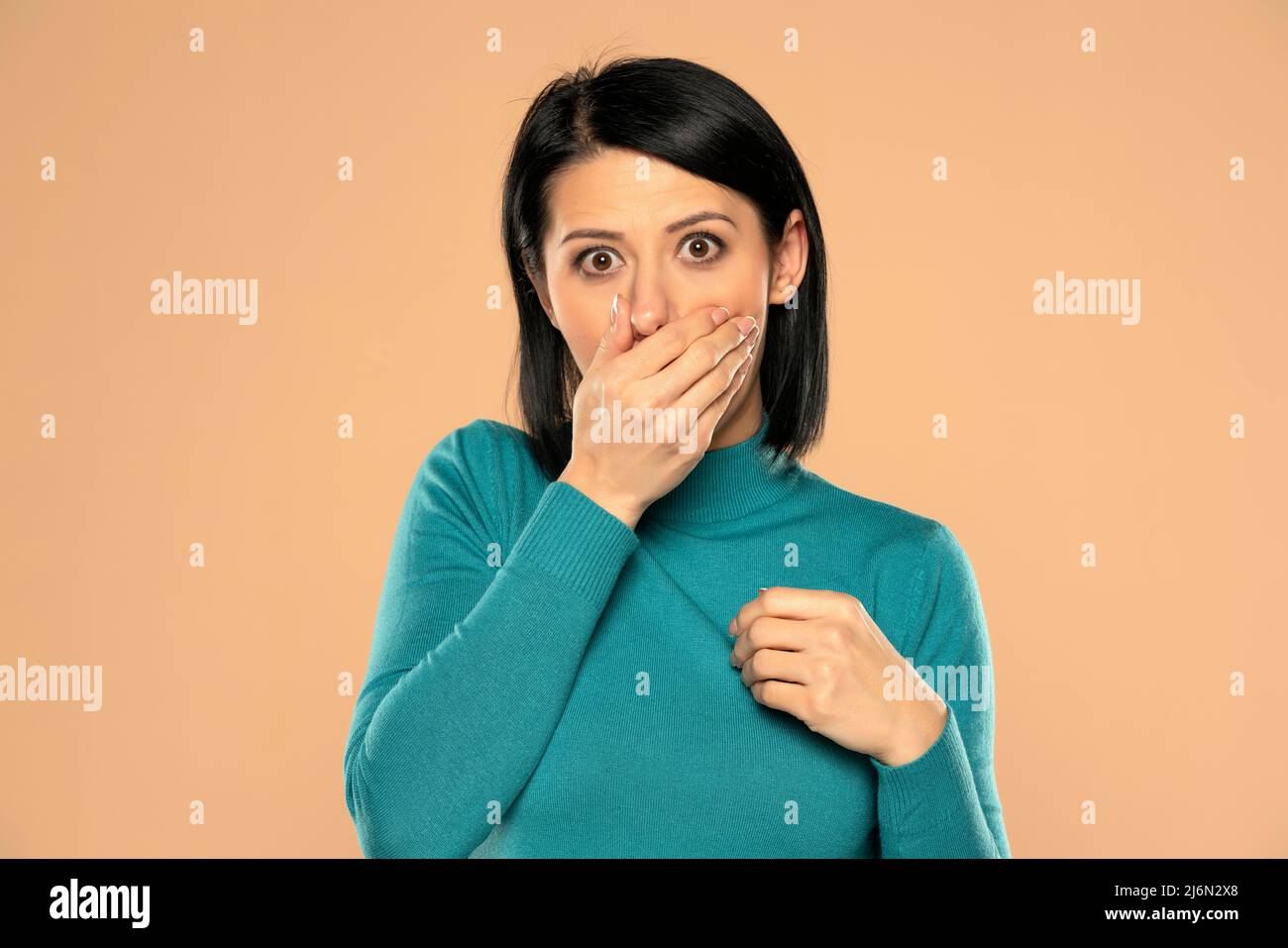 Middle aged woman covers her mouth with her hand on a beige background ...