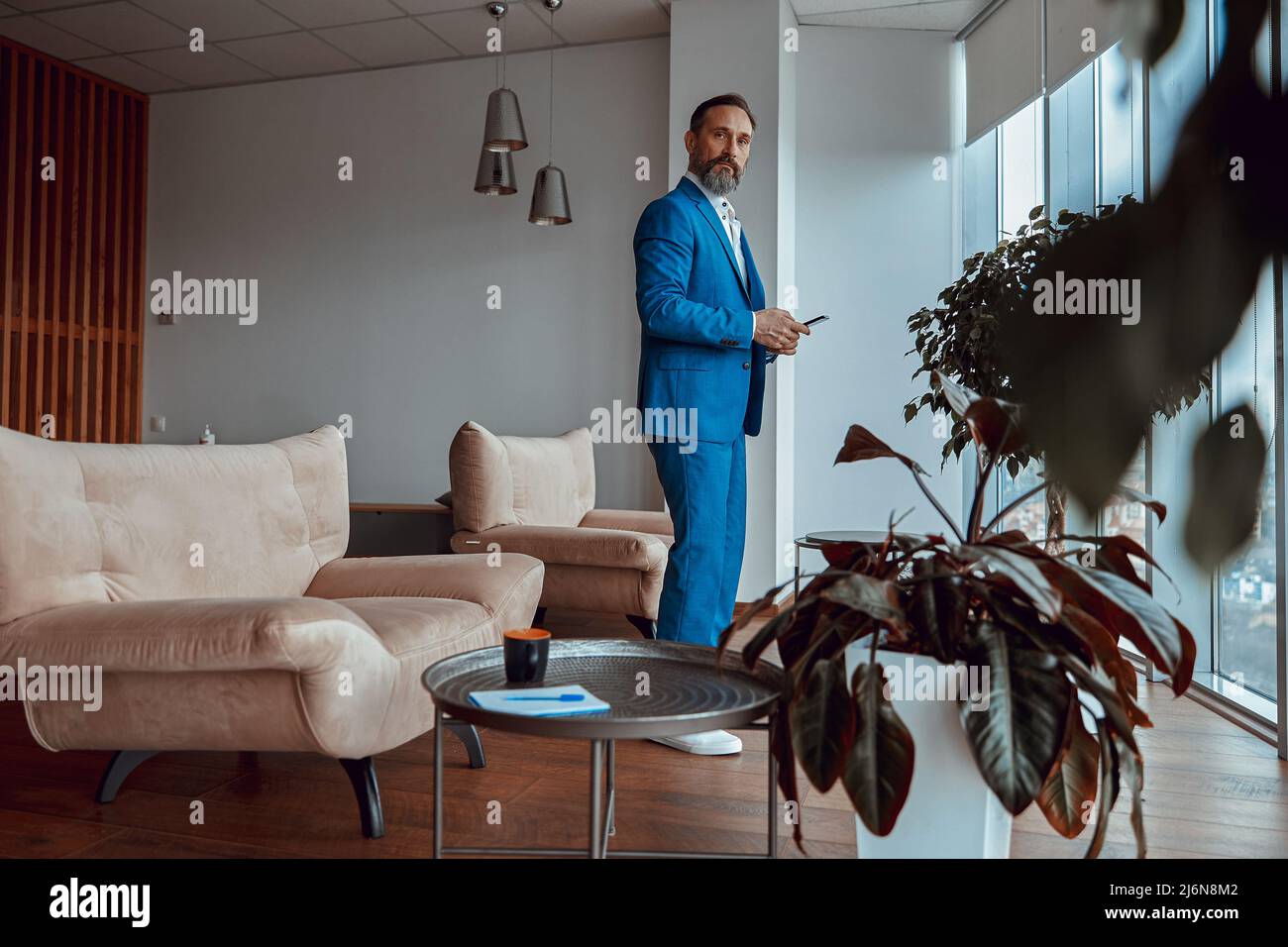 Happy stylish man with smartphone standing in modern lobby Stock Photo ...