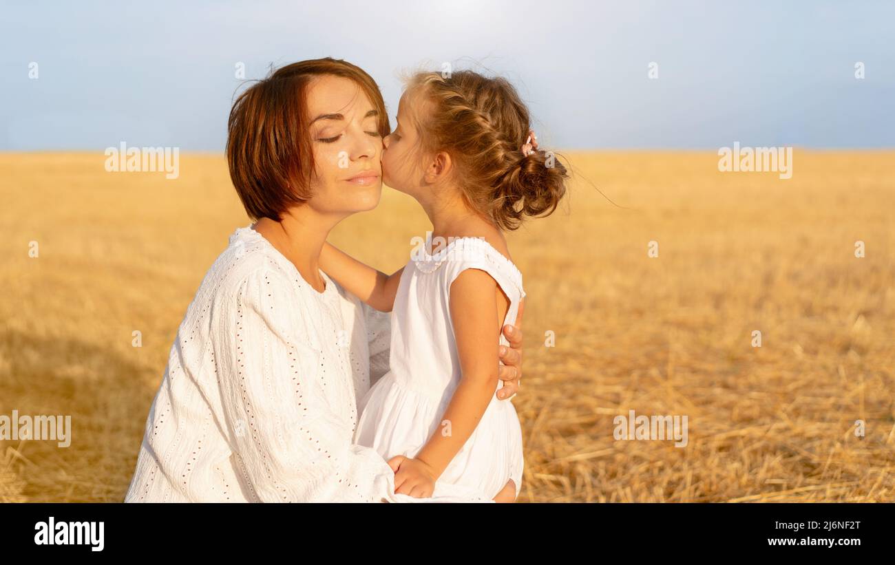 Daughter kisses her mom cheek standing wheat field. Little girl kiss ...