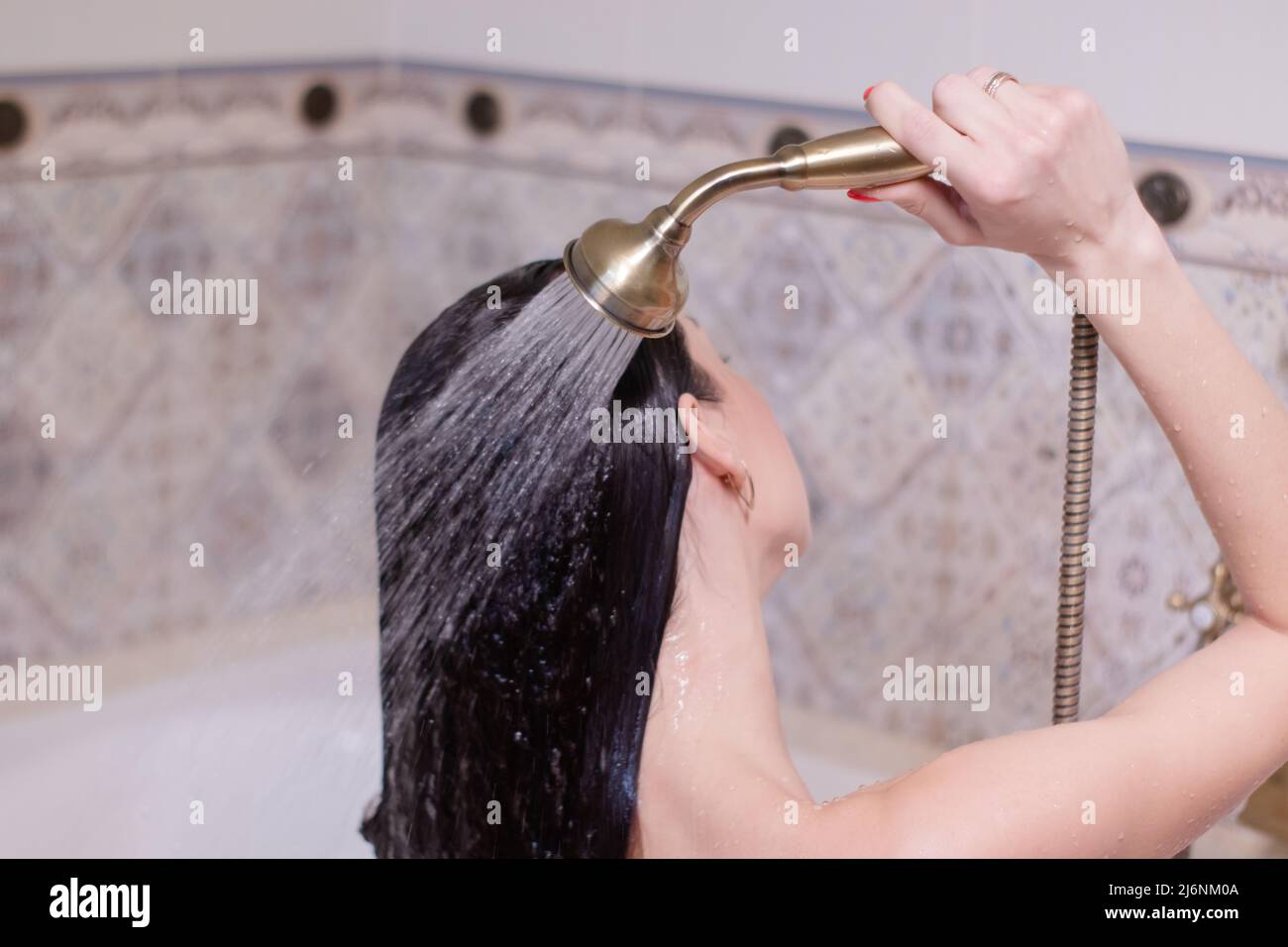 Young brunette woman washing her long hair under the shower standing ...