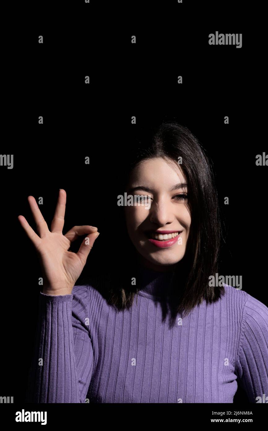 brunette woman doing the ok symbol winking an eye on black background ...