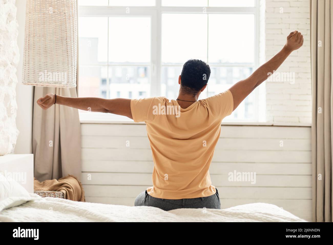 Man Sitting On Bed Stretching Arms In Bedroom, Back View Stock Photo ...