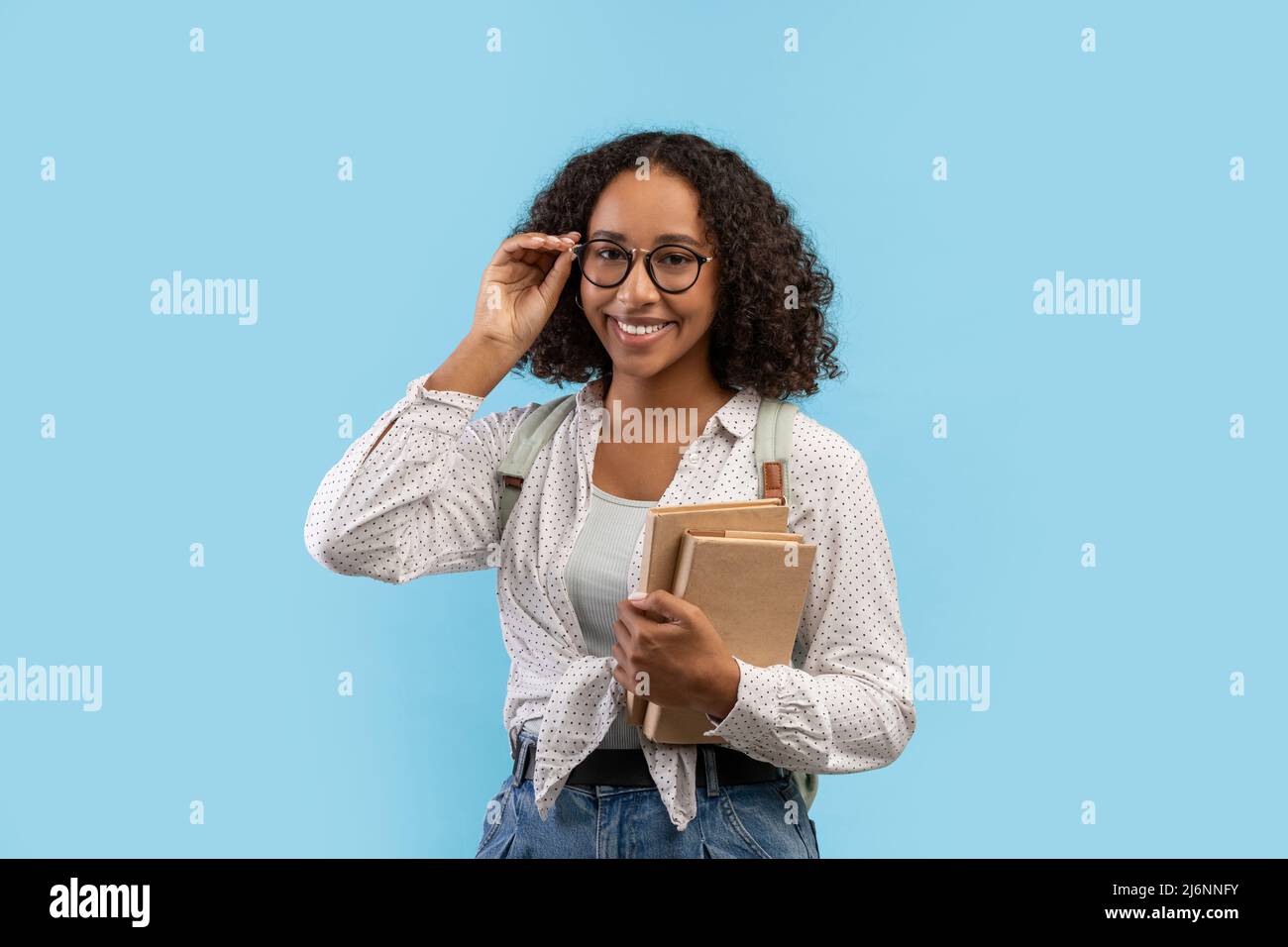 Portrait of young black female student with books touching glasses and ...