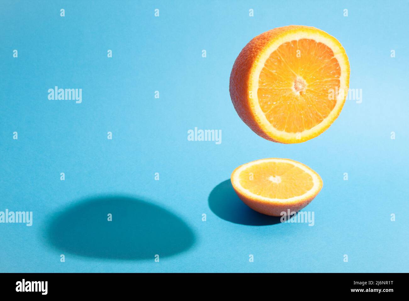 Half of orange flying on blue background with hard shadow on surface ...