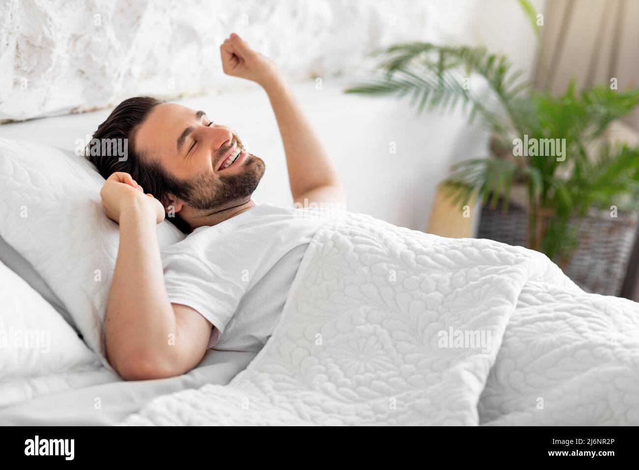 Side view of smiling young man stretching in bed Stock Photo - Alamy