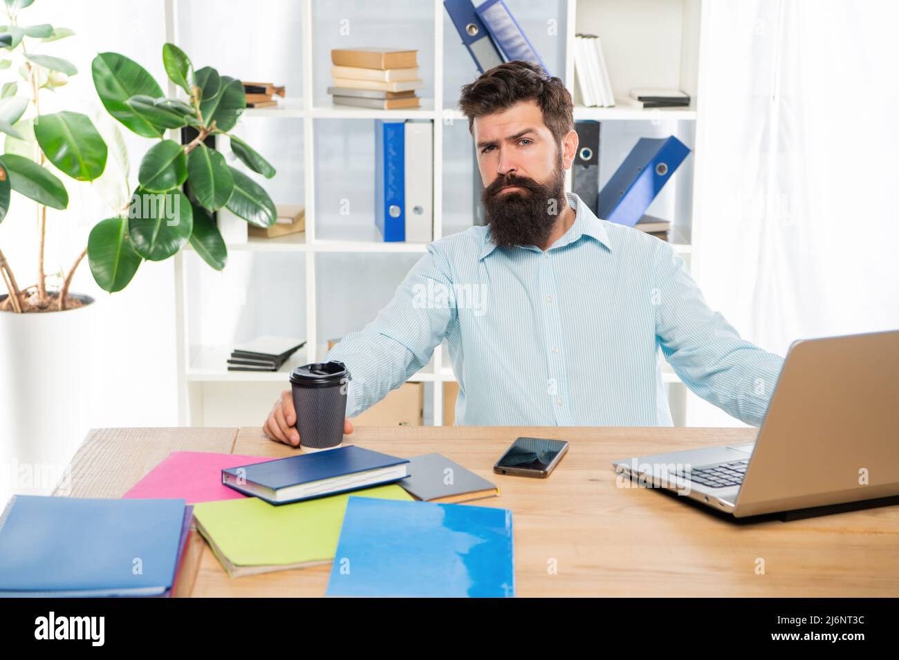 Tired guy drinking takeaway coffee working at office desk, coffee break ...