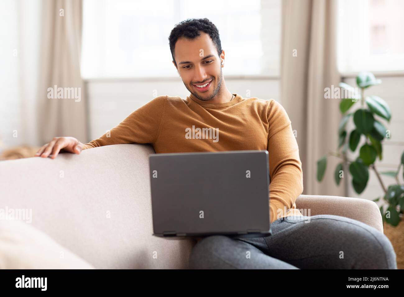 Arab man using laptop sitting on couch at home Stock Photo - Alamy